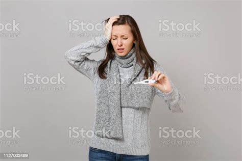 닫힌된 눈을 가진 스웨터 스카프에 피곤된 여자 마 보류 온도계 회색 배경에 고립에 손을 넣어 건강 한 라이프 스타일 아픈 아픈
