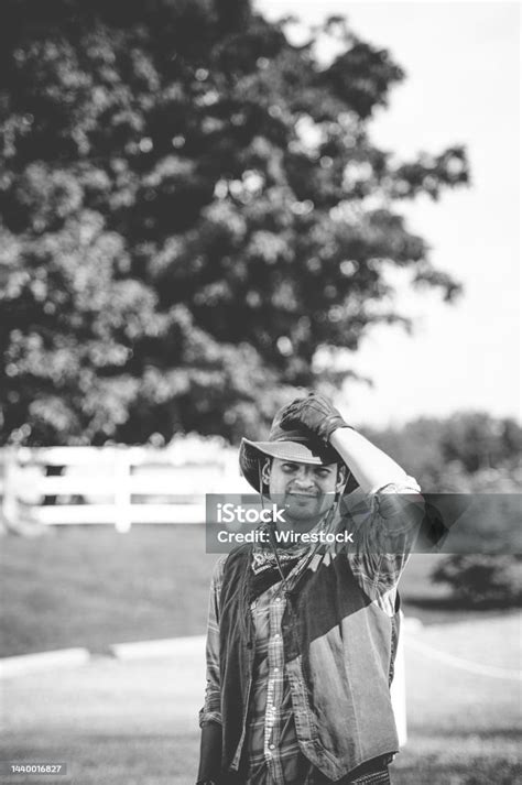 카우보이 복장을 한 남성의 세로 회색조 샷이 모자에 손을 얹고 있습니다 개척시대의 서부에 대한 스톡 사진 및 기타 이미지