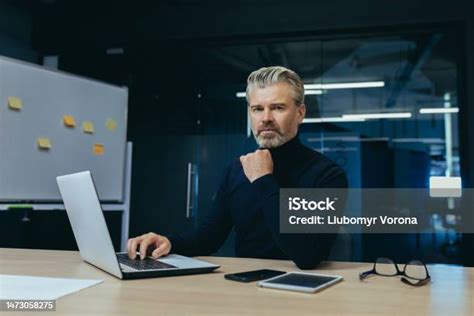 심각한 회색 머리 상사 카메라 사고를 보고 있는 남자 직장에서 노트북을 사용하여 책상에서 일하는 사무실 내부의 성숙한 사업가의 초상화 40 44세에 대한 스톡 사진 및 기타