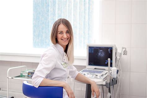 클리닉 병원에서 흰색 유니폼을 입은 금발의 여성 의사가 초음파 스캐너에서 작동하고 카메라에서 미소 진단 초음파 및 건강 개념 카피스파제 Stem 주제에 대한 스톡 사진 및