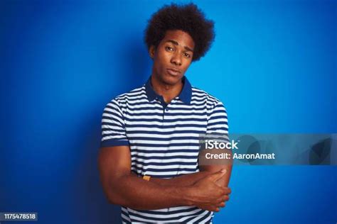 고립 된 파란색 배경 회의적이고 긴장한 위에 서있는 줄무늬 폴로를 입은 아프리카 계 미국인 남성은 교차 된 팔로 얼굴에 표정을 거부합니다 부정적인 사람 감정에 대한 스톡