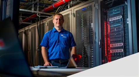 Male It Technician Running Maintenance Programme On A Laptop Controls Operational Server Rack