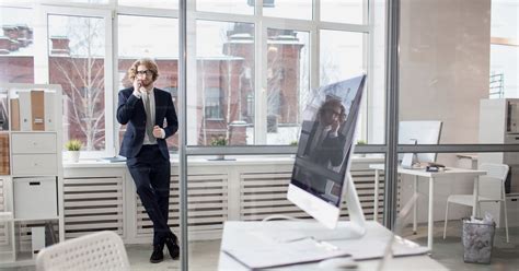 정장을 입은 젊은 우아한 사업가가 사무실의 창가에 서서 스마트폰으로 말하는 사진 Unsplash의 실내 이미지