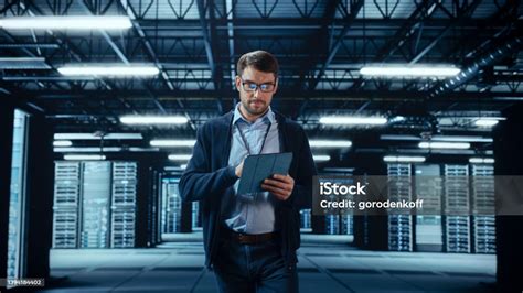 남성 It 전문가가 데이터 센터의 운영 서버 랙 행 사이를 안내합니다 엔지니어는 유지 보수를 위해 태블릿 컴퓨터를 사용합니다 클라우드 컴퓨팅 인공 지능 사이버 보안에 대한