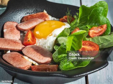 검은 둥근 냄비에 소시지 체리 토마토와 잎 양상추와 스크램블 계란의 풍부한 아침 식사 빵 빵과 테이블 포크와 보드 트레이에 제공 합니다 가까운 거리에서 촬영 측면 보기 0