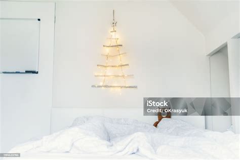 간단하고 최소한의 양심적 인 크리스마스 인테리어 디자인 장난감 곰침대 위의 흰색 벽에 화환이있는 나무 막대기로 만든 특이한 크리스마스 트리 소프트 선택적 초점 공간을