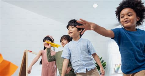혼혈 어린 아이가 교실에서 비행기를 타고 있다 어린 소녀와 소년 학생은 학교 교실에서 함께 즐거운 시간을 보내면서 휴식 시간에 종이 로켓을 연주합니다 사진