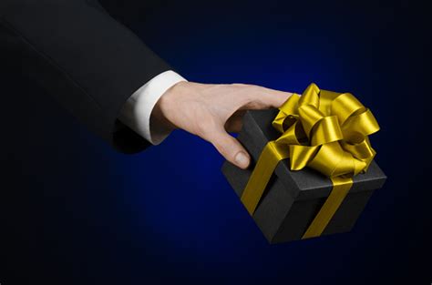 축 하와 선물의 테마 절연 스튜디오에 진한 파란색 배경에 골드 리본 아름 다운 블랙 박스에 포장 하는 독점적인 선물 비싼 선물을 들고 검은 양복에 남자 검은색에 대한 스톡