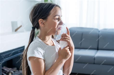 아픈 어린 소녀는 복사 공간이 있는 회색 배경 위에 흡입을 합니다 집에서 분무기로 흡입하는 소녀 어린이 천식 흡입기 흡입