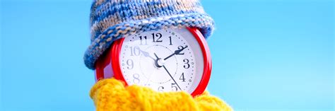 니트 울 블루 모자와 파란색 배경에 노란색 스카프빨간색 둥근 알람 시계 겨울 시간 개념 겨울 아늑하고 따뜻한 아날로그 시간 1010 텍스트 공간을 사용할 수 있습니다 배너