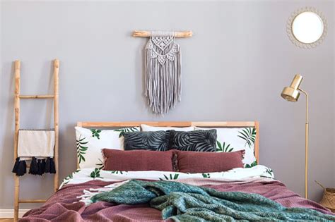 디자인 가구 세련 된 Macrame 나무 사다리 금 램프와 우아한 액세서리와 침실의 현대적이 고 고급 스러운 인테리어 아름 다운 침대 시트 담요 및 베개 따뜻하고 세련 된