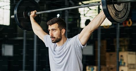 체육관에서 크로스 트레이닝을 하는 동안 스쿼트를 하는 동안 머리 위로 바벨을 들고 있는 남자 운동선수 사진 Unsplash의 웅크리다 이미지