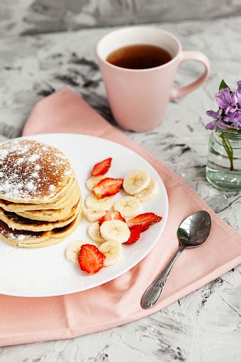 밝은 배경에 흰색 접시에 분홍색 차 찻잔과 신선한 딸기가있는 팬케이크 더미 아침 식사 옆에는 유리 꽃병에 담긴 작은 라일락 꽃다발이 있습니다 건강한 생활방식에 대한 스톡