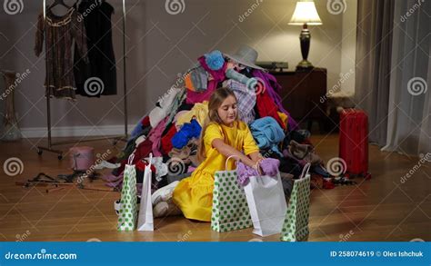 Cute Caucasian Teen Girl Sorting Clothes In Shopping Bags Sitting In Living Room At Pile Of