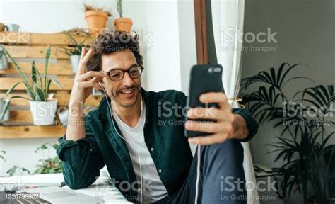 집에서 원격으로 작업하는 노트북과 스마트 폰을 가진 남자는 휴대 전화로 화상 통화를합니다 원격 작업에서 프리랜서 아늑한 직장 35 39세에 대한 스톡 사진 및 기타 이미지