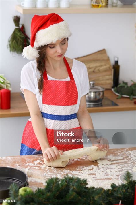 부엌에서 산타 클로스 모자를 착용하는 동안 피자 또는 수제 파스타를 요리 하는 젊은 갈색 머리 여자 나무 테이블에 반죽을 준비하는 주부 땋은 머리에 대한 스톡 사진 및 기타