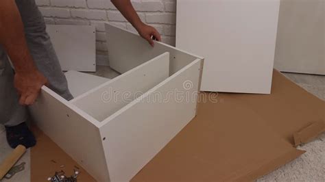 A Man Is Assembling A Bookshelf Attaches The Side Walls With A Key