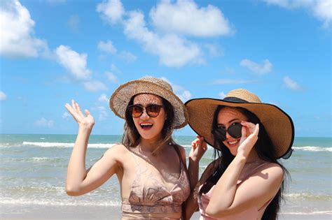 큰 모자와 선글라스를 가진 두 명의 아름다운 아시아 여성은 열대 모래 해변 푸른 바다에서 친구와 함께 시간을 보내고 여름 휴가에서 휴식을 취합니다 25 29세에 대한 스톡