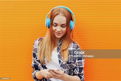 오렌지 배경에 캐주얼 옷을 입고 음악을 듣고 무선 헤드폰에 전화를 가진 예쁜 여자 스마트폰에 대한 스톡 사진 및 기타 이미지 스마트폰 20 24세 20 29세