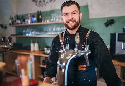 검은 유니폼을 입고 앞치마를 두르고 생맥주 탭이 있는 바 카운터에서 행복하게 웃는 수염 바텐더의 초상화 성공한 사람들 노력 소비자 카페 및 레스토랑 산업 개념 35 39세에