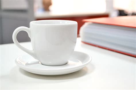 커피 휴식 빨간색 파일 폴더와 하드 커버 근처의 흰색 사무실 책상에 차 또는 커피를위한 흰색 컵 컵은 작업 공간에서 비어 있습니다 흐릿한 사무실 공간의 배경에 대해 0명에