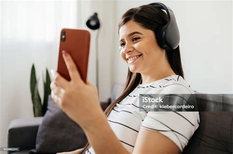 소파에 앉아 거실에서 집에서 스마트 폰으로 음악을 듣는 웃는 소녀 25 29세에 대한 스톡 사진 및 기타 이미지 25 29세 Brand Name Smart Phone