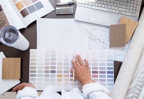 캐주얼 웨어를 입은 인테리어 디자이너나 건축가가 새로운 프로젝트의 청사진을 작업하고 낮에 사무실에 서 있는 모습 노트북 컬러 샘플 커피 컵 도구 색상 견본에 대한 스톡 사진