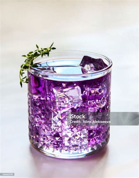 보라색 주류와 얼음 조각과 백리향 나뭇 가지가있는 소다로 만든 투명한 유리에 담긴 보라색 칵테일 밝은 회색 배경에 자연광에서 완벽하게 매끄러운 표면을 가진 다채로운 상쾌한