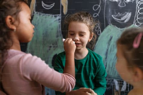 놀이방 실내에서 다른 소녀의 뺨에 분필로 그림을 그리는 어린 소녀 사진 Unsplash의 예술 이미지