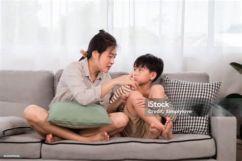 사랑스러운 아들의 상처를 다친 무릎에 부드럽고 정성스럽게 치료하는 아시아의 어머니 아이가 아플까 봐 걱정되는 싱글맘 건강과 의학 개념 가족 안에서의 사랑과 보살핌 아이에