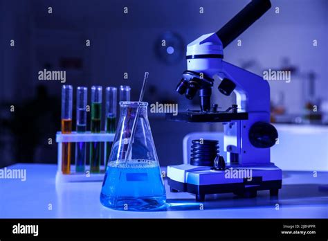Modern Microscope And Conical Flask With Liquid On Table In Medical