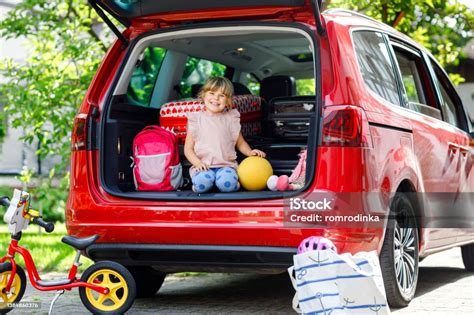 부모와 함께 여름 휴가를 떠나기 전에 자동차 트렁크에 앉아 귀여운 작은 유치원 소녀 여행 가방 자전거 및 장난감이있는 행복한 활동적인 아이가 가족 여행 도로 여행 차에 대한