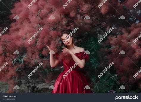 زن زیبا با لباس قرمز در حال قدم زدن در باغ پر از گل رز 1623163