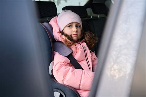 매력적인 귀여운 어린 아이 분홍색 따뜻한 옷을 입은 귀여운 베이비 소녀는 자동차로 가족 겨울 여행 중에 현대적인 차에 안전한 안전 벨트로 고정되어 있습니다 어린이와 함께