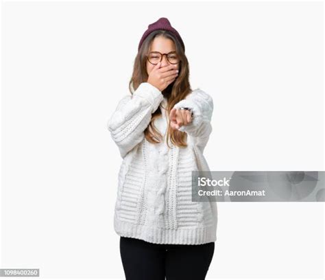 격리 된 이상 안경 및 겨울 모자를 입고 젊은 아름 다운 갈색 머리 Hipster 여자 배경 당신의 입 부 끄 러운 식 이상 손가락 손으로 카메라를 가리키는 웃음 가리키기에