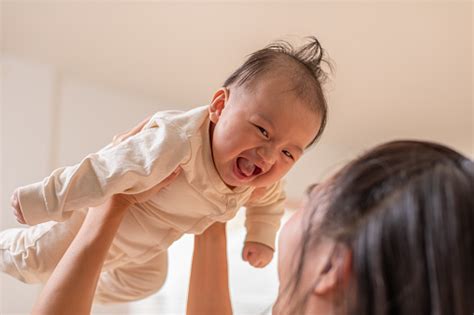 행복한 사랑스러운 신생아는 아늑한 집에서 미소와 쾌활한 침대에서 엄마와 놀고 있습니다 엄마는 함께 공중에 신생아를 던지는 웃는 유아 아기와 이야기 시간을 휴식 아기와