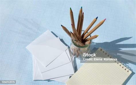 유리 항아리에 색연필 메모용 흰색 시트와 케이지에 시트가 있는 노트북을 비우고 있습니다 연필 항아리에서 그림자 텍스트공간을