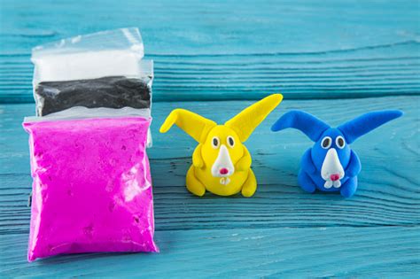 노란색과 파란색의 두 개의 부활절 토끼가 밝은 파란색 나무 배경에 플라스틱으로 만들어졌습니다 여러 가지 색상의 플라스틱 포장 옆에 있습니다 행복한 부활절 가방에 대한 스톡