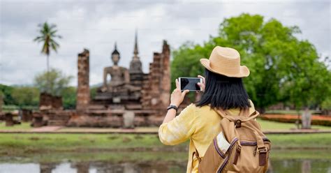 아시아 관광 여성은 모바일을 사용하여 태국 수코타이 Sukhothai에서 태국 건축물의 고대 탑 사원 사진을 찍습니다 캐주얼 태국 옷감 스타일의 여성 여행자 방문 도시