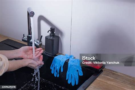 부엌 싱크대에서 흐르는 물에 손을 담그고 거품 스펀지와 청소 작업을 위한 고무 장갑을 포함한 청소 용품을 근처에 둡니다 가사 집안일에 대한 스톡 사진 및 기타 이미지