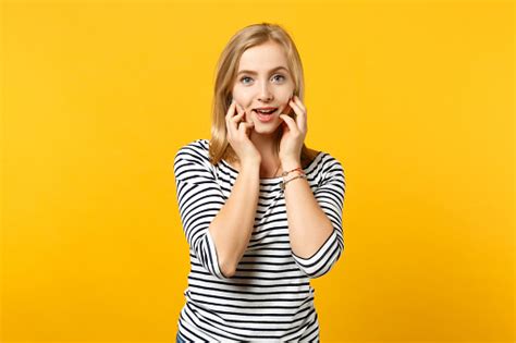 스튜디오에서 노란 주황색 벽 배경에 고립 된 뺨에 손을 넣어 카메라를 찾고 줄무늬 옷에 아름 다운 젊은 여자 사람들은 진심으로 감정 라이프 스타일 개념입니다 복사 공간을