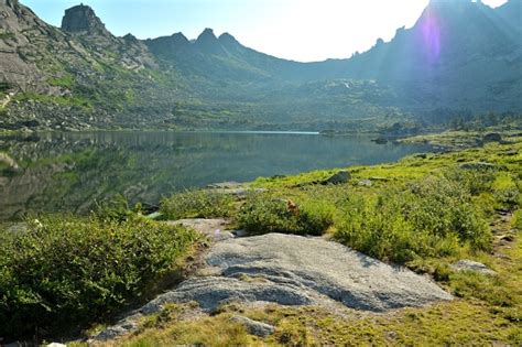 떠오르는 태양의 광선은 화창한 여름 아침에 높은 산으로 둘러싸인 아름다운 큰 호수가 있는 그림 같은 계곡을 비춥니다 0명에 대한