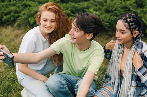 어린 소년은 친구들과 함께 스마트폰 카메라로 비디오를 만들고 해질녘 공원에서 야외에서 함께 비디오를 만들고 있다 소셜 미디어 응용 프로그램에 비디오를 공유합니다 휴대 전화