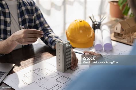 엔지니어 팀 회의와 노트북을 사용하여 이야기하고 사무실에 노란 모자 집 모델이 있는 테이블에 있는 청사진과 서류 프로젝트 관리자가 동료와의 회의에 대해 논의합니다 개발에