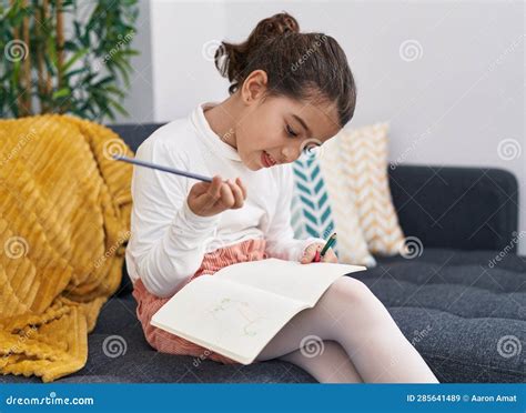 Adorable Hispanic Girl Drawing On Notebook Sitting On Sofa At Home