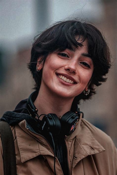 A Smiling Woman With Headphones On Her Ears And Wearing A Brown Jacket