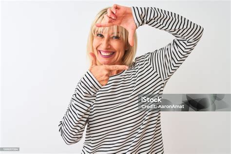 해군 줄무늬 티셔츠를 입은 중년 여성이 고립 된 흰색 배경 위에 서서 행복한 얼굴로 손과 손가락으로 프레임을 만드는 미소 창의력과 사진 개념 T 셔츠에 대한 스톡 사진 및