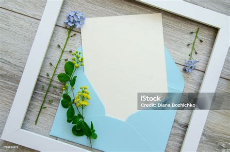 정사각형 흰색 나무 프레임과 파란색 봉투 흰색 엽서 Copyspace 작은 파란색과 노란색 꽃과 가지에 녹색 잎이 있는 회색 천연 나무 배경 가정 생활에 대한 스톡 사진 및