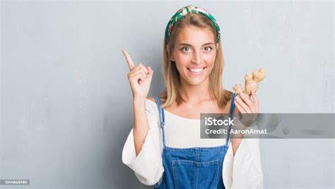 그런 지 회색에 아름 다운 젊은 여 자가 놀 생각으로 신선한 생강을 들고 벽 또는 행복 한 얼굴 넘버 원 가리키는 손가락 질문