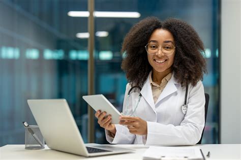현대적인 사무실 환경에서 태블릿을 사용하고 미소를 지으며 청진기를 착용하고 효율적인 의사 소통과 환자 참여를 위한 의료 기술을 홍보하는 자신감 넘치는 아프리카계 미국인 여성